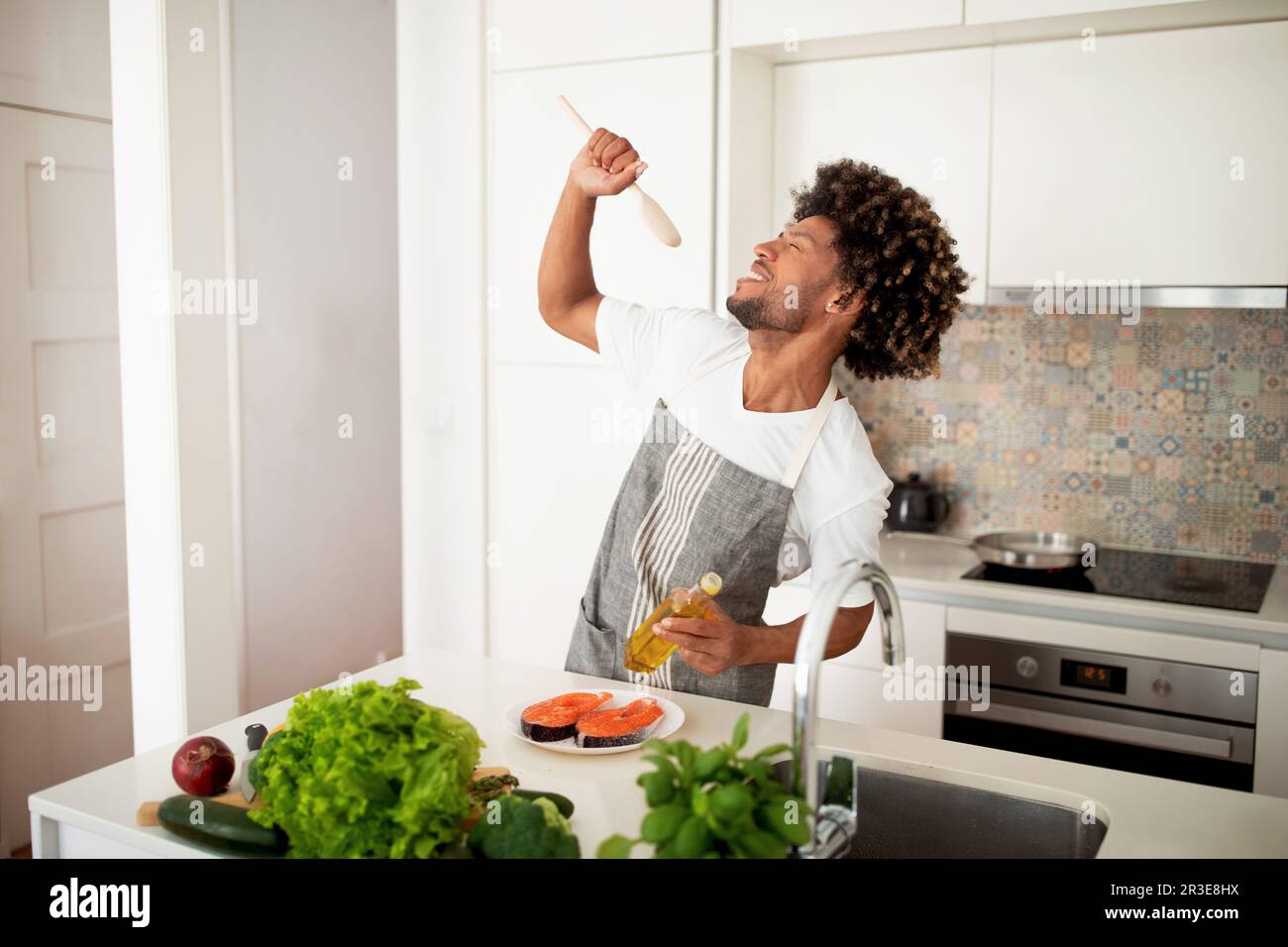 Black Cook Man Singing With Spoon In Hand In Kitchen Stock Photo - Alamy