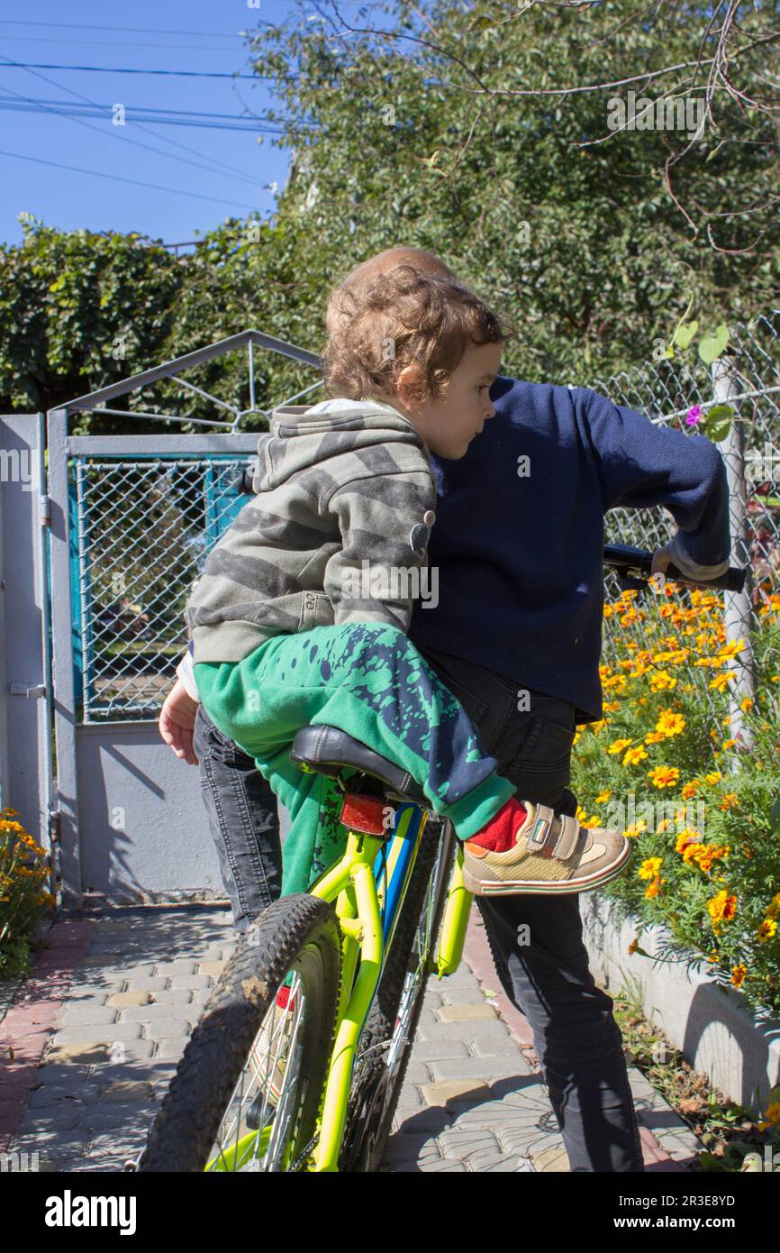 the younger brother sits on a bike to his elder brother, riding a ...