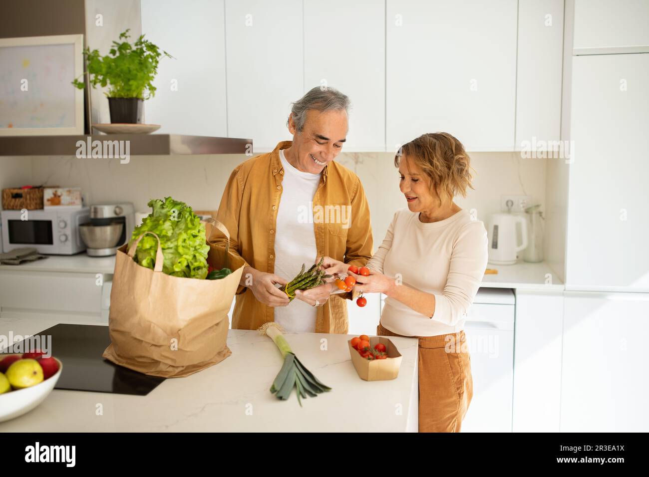 Aged married spouses unpacking paper bag from supermarket, enjoying ...