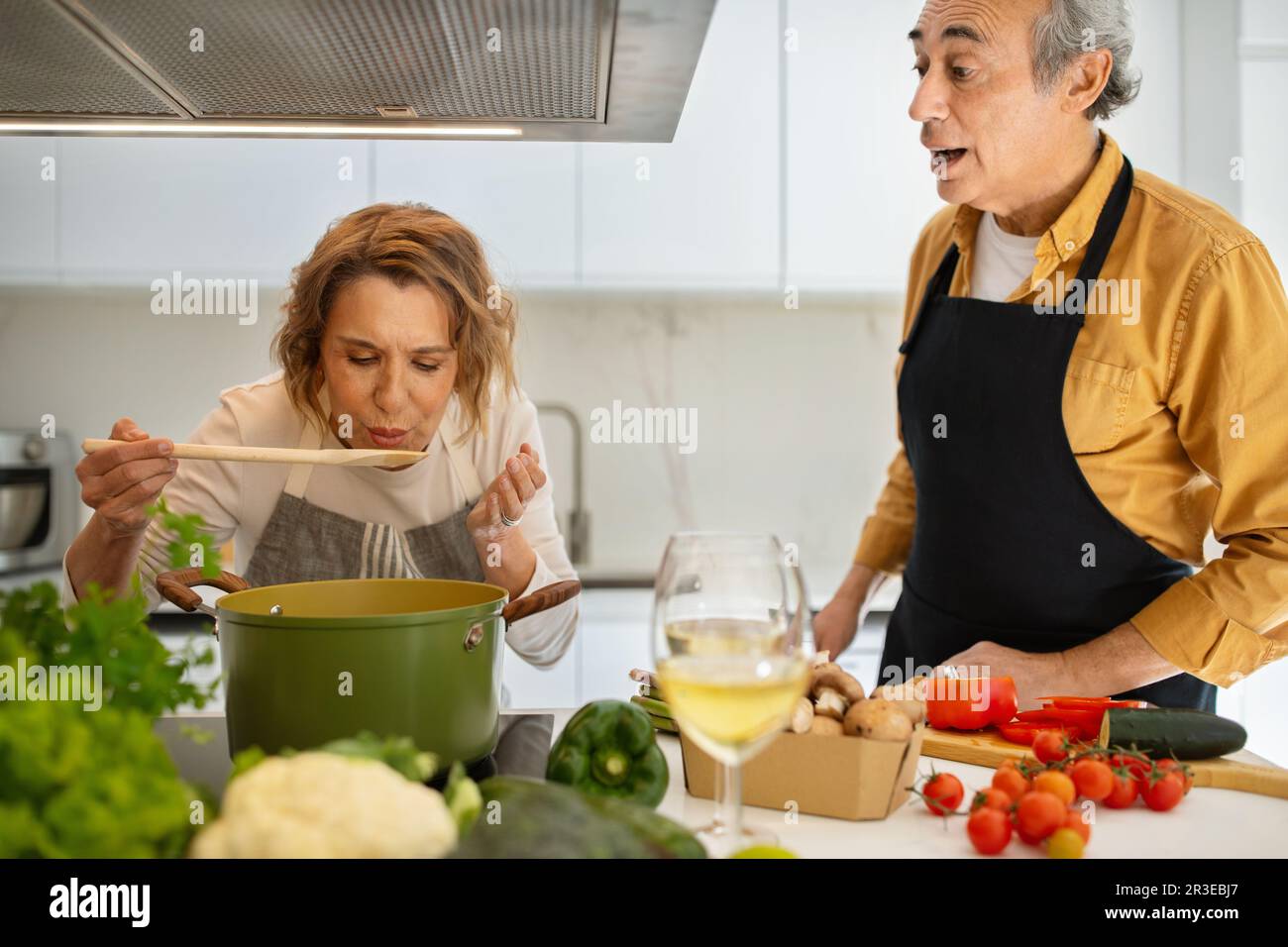 Elderly spouses cooking lunch together in kitchen, elderly wife trying ...