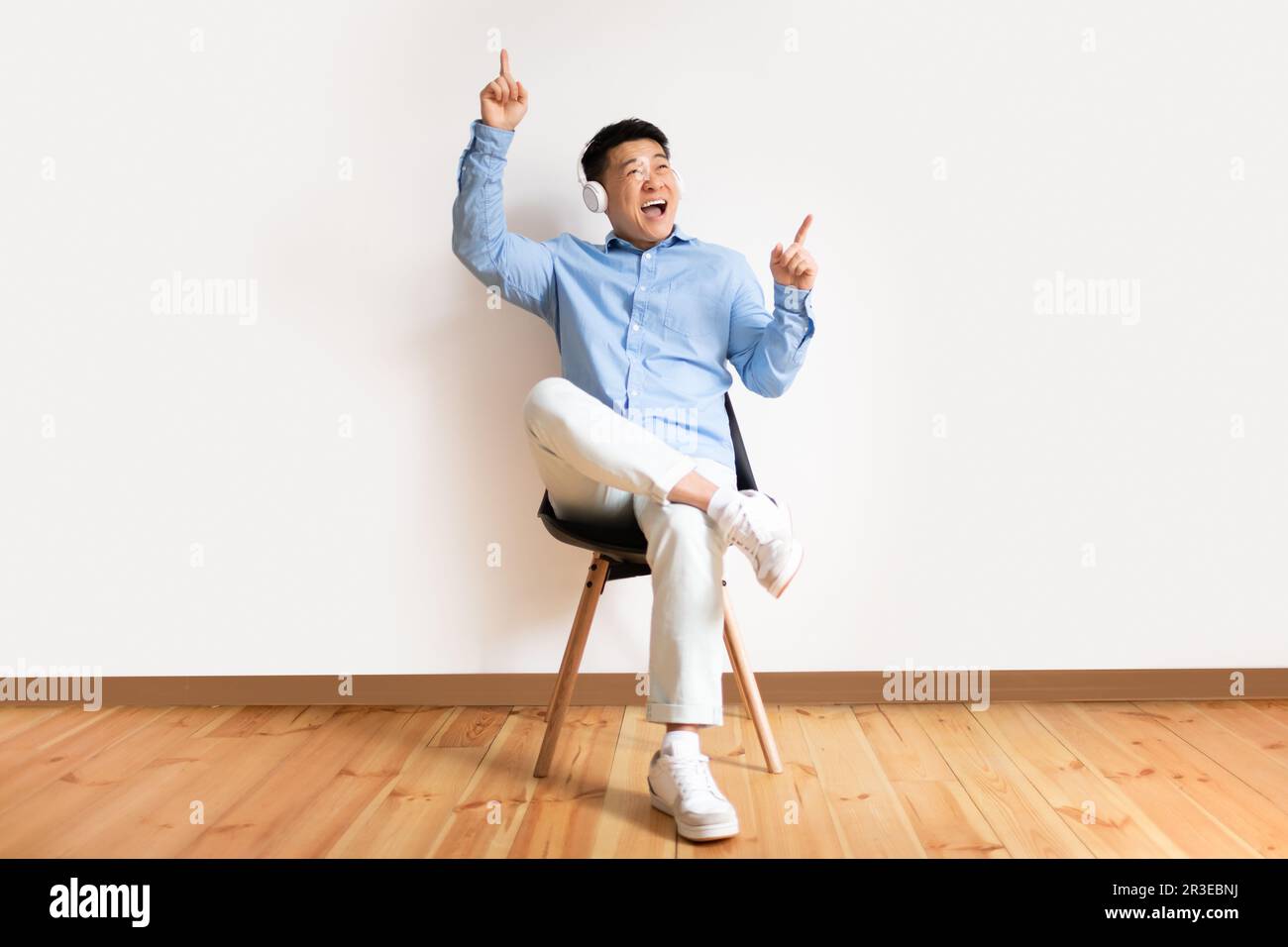 Cool asian middle aged man sitting on chair over light wall, listening ...
