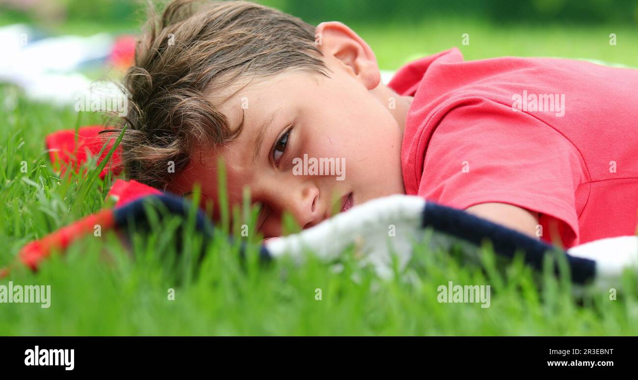 Young handsome child boy lying down on grass outdoors, kid resting and ...