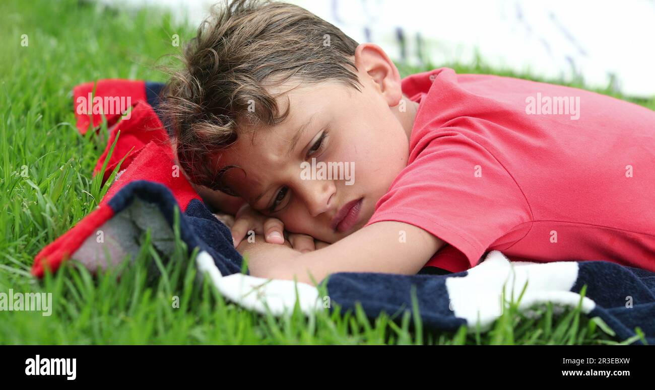 Pensive child lying on grass outside. Thoughtful young boy thinking ...