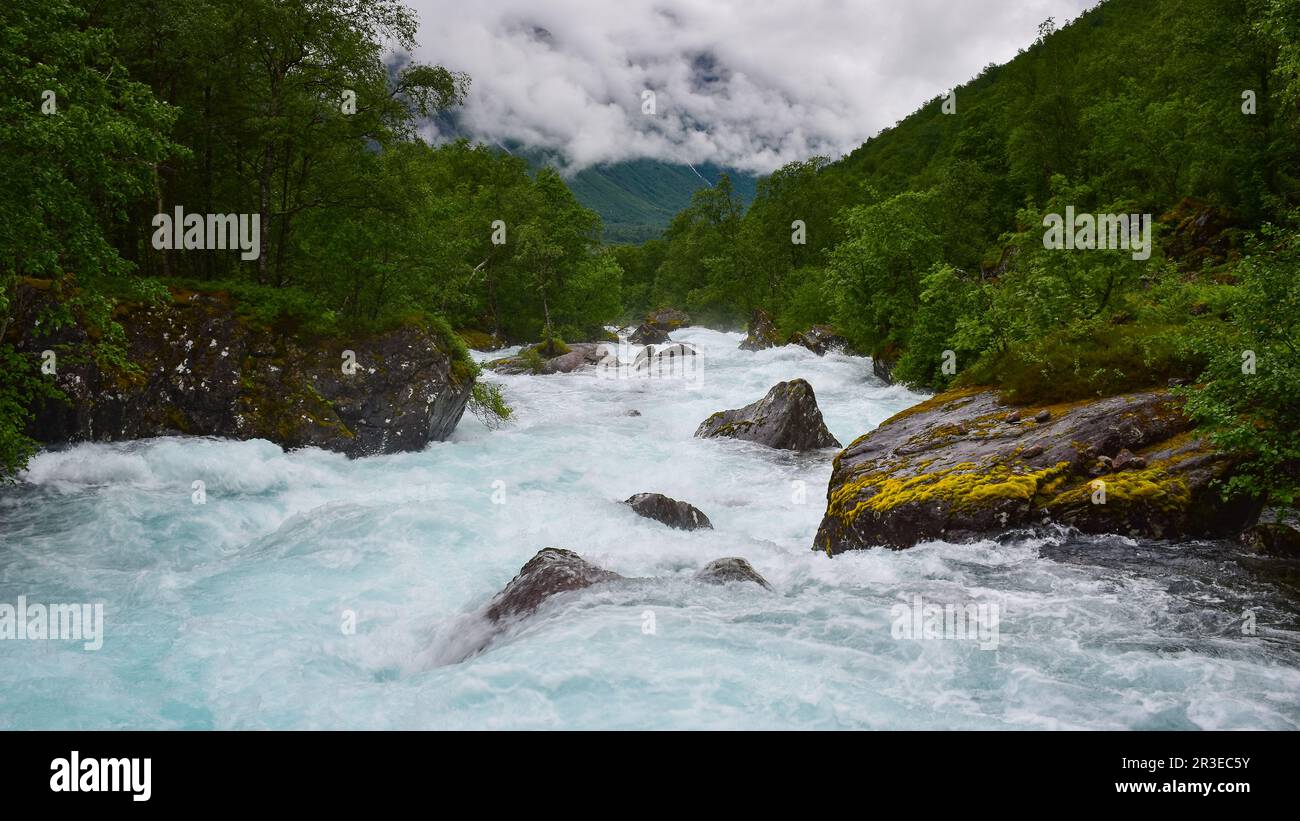 Rocks washed over by strong river rapids water, clouds shrouding ...