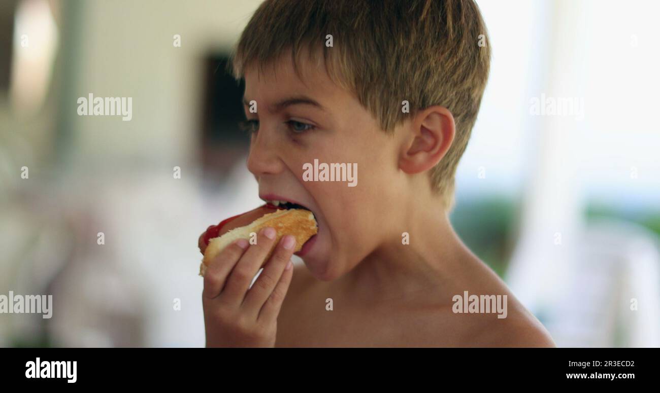 Young boy child taking a bite of hot-dog. Kid eating junkfood snack ...