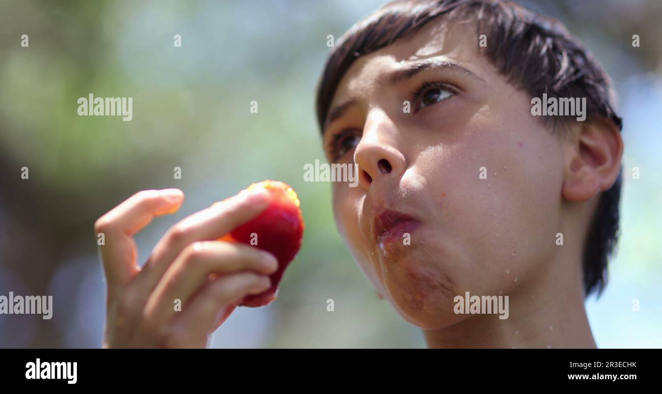 Young boy taking a bite of healthy peach fruit outside. Healthy diet ...