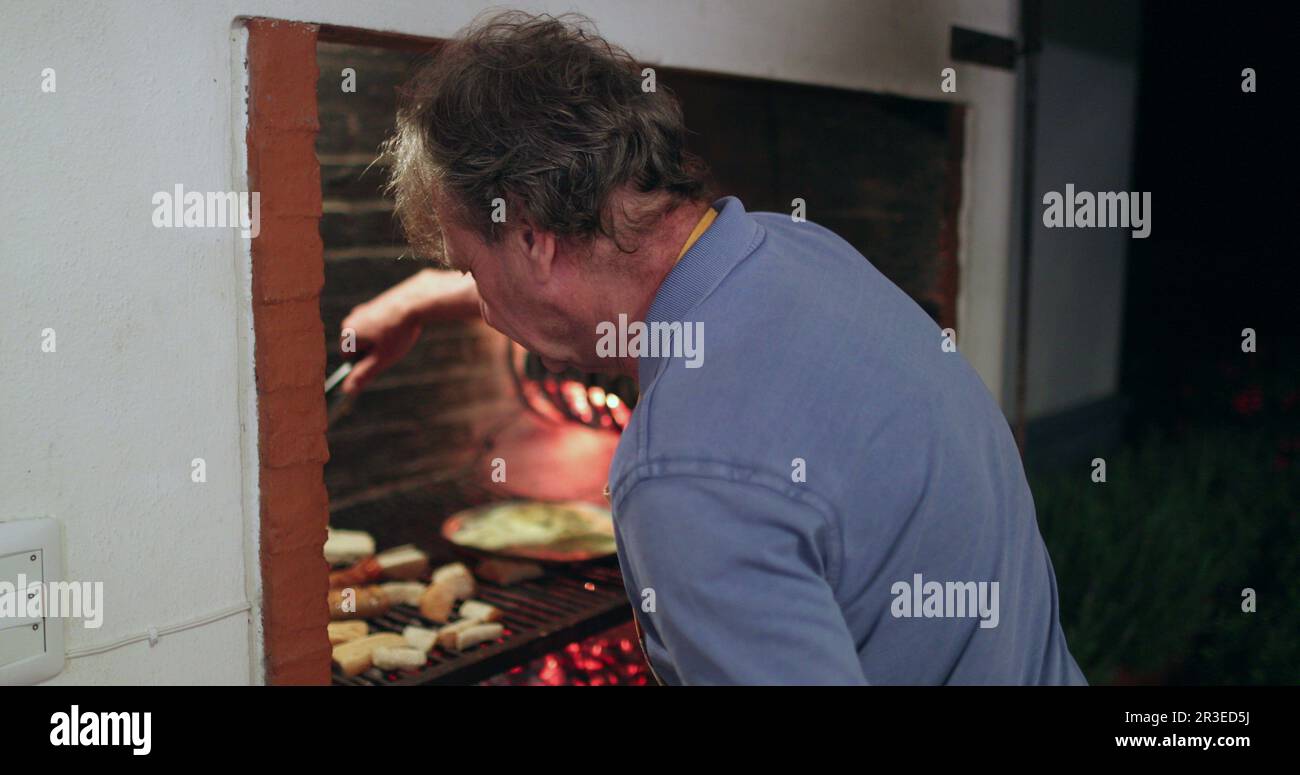 Retired older man managing grill BBQ parilla at night. Senior man ...