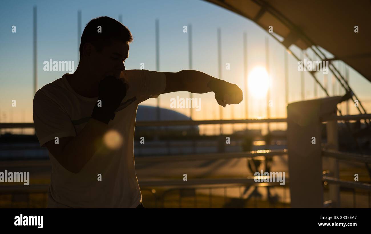 A man trains in boxing at the stadium at sunset. Athlete silhouette ...