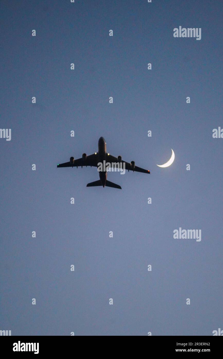 London UK. 23 May 2023 A commercial airplane flies under a crescent ...