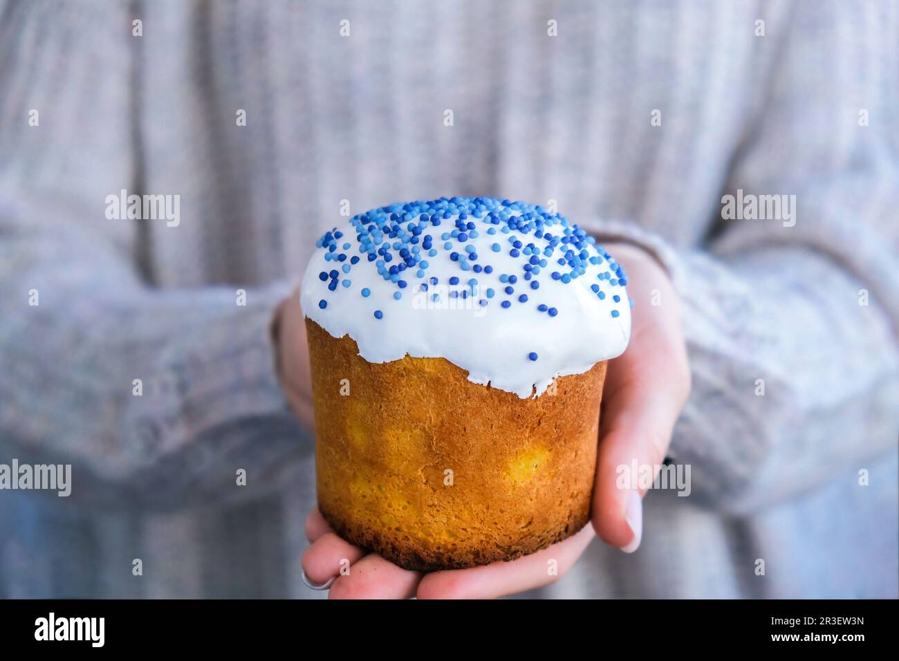 Hands hold Easter cake with white topping and blue sprinkles. Woman ...