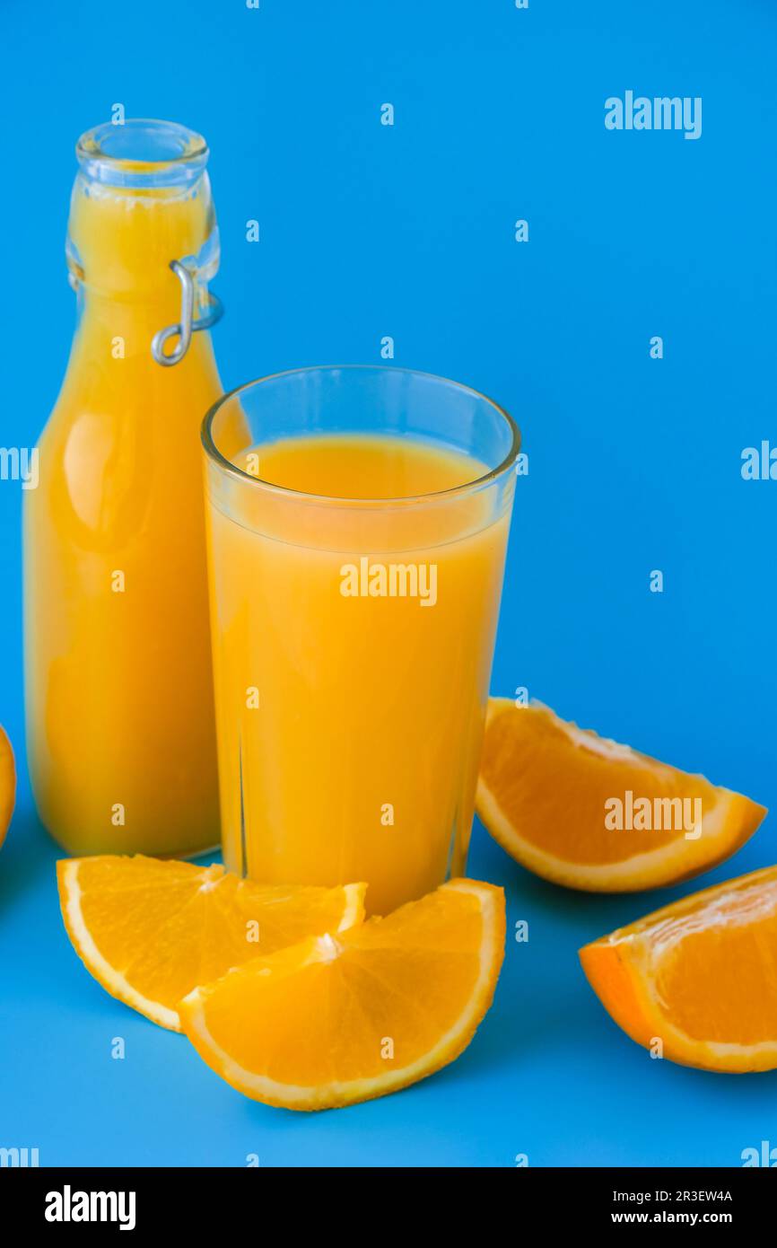 Glass bottle of fresh squeezing Orange juice with sliced fruits on blue ...