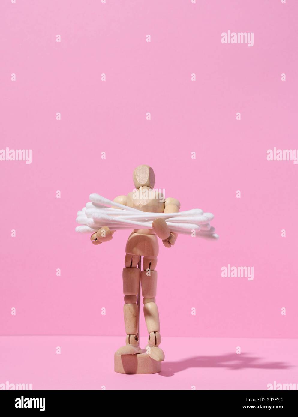 Wooden mannequin holding a stack of ear sticks on a pink background ...
