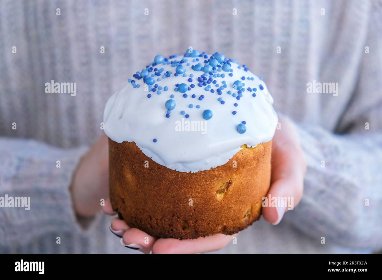 Hands hold Easter cake with white topping and blue sprinkles. Woman ...