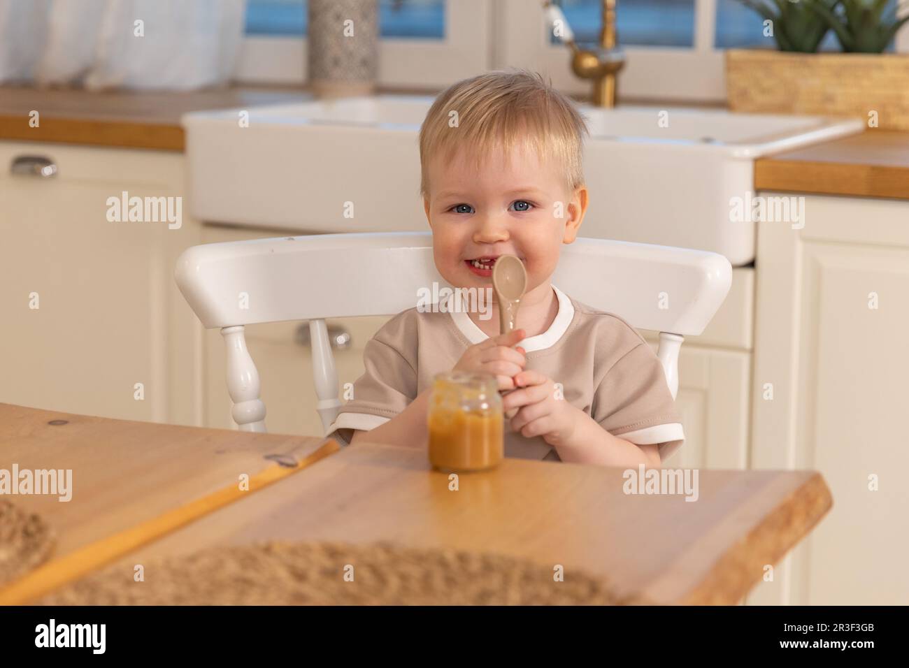 Happy family at home. Baby boy feeding himself in kitchen. Little boy ...