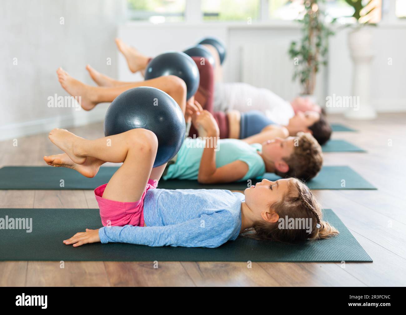 Children and parents practice yoga and Pilates using soft ball in gym ...