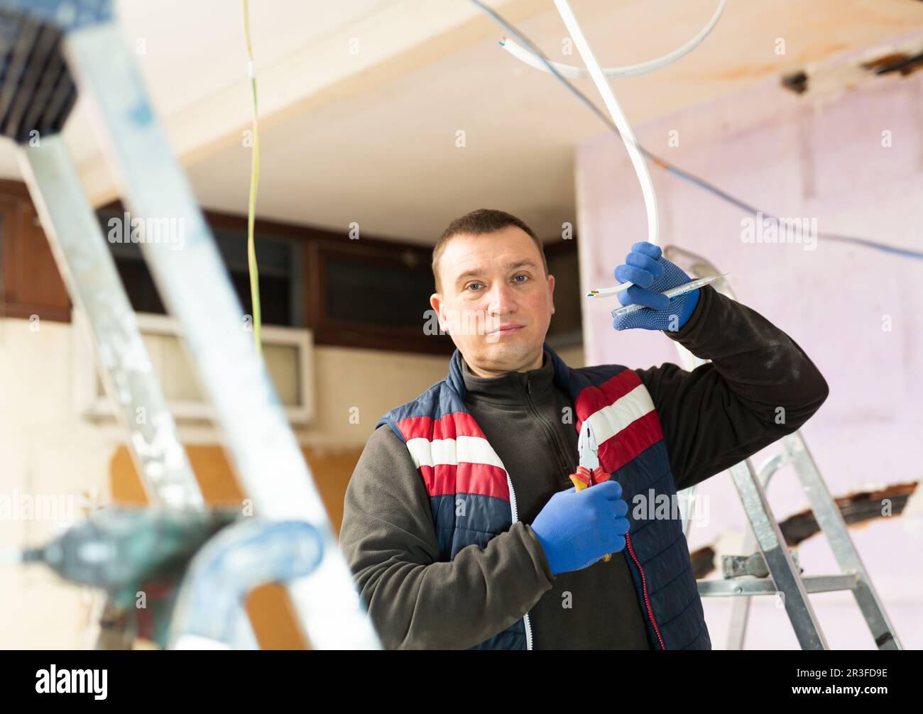 Electrician with pliers in hand prepares electrical wiring in house ...