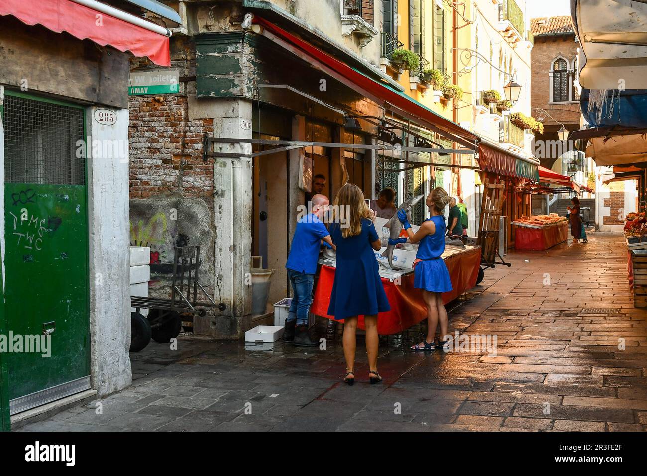 Two young foreign tourists are jokingly chatting with a fishmonger who ...