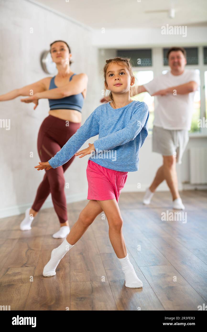 Cute little girl practicing dance movements with her family members ...