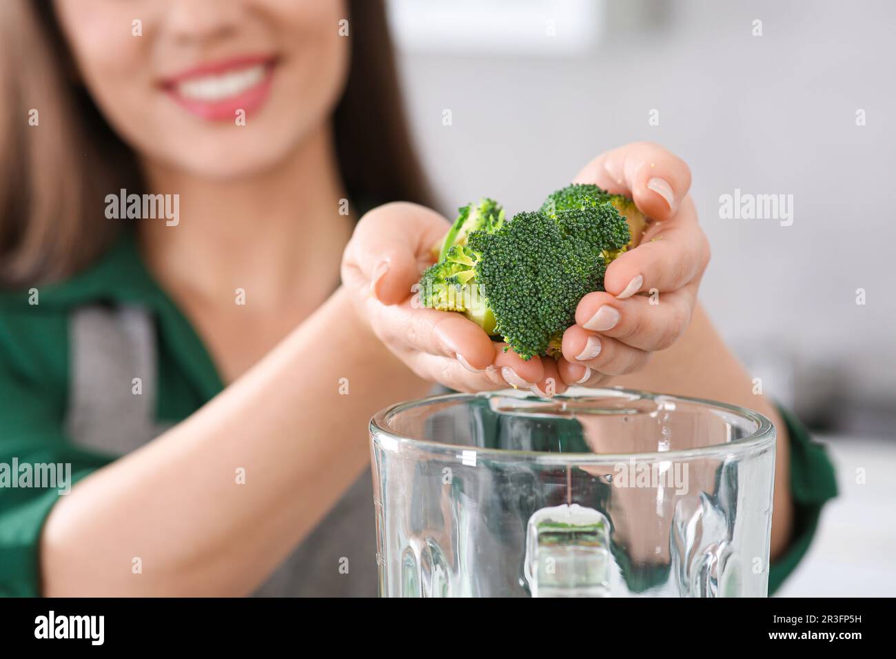 Woman adding broccoli into blender for smoothie on blurred background ...