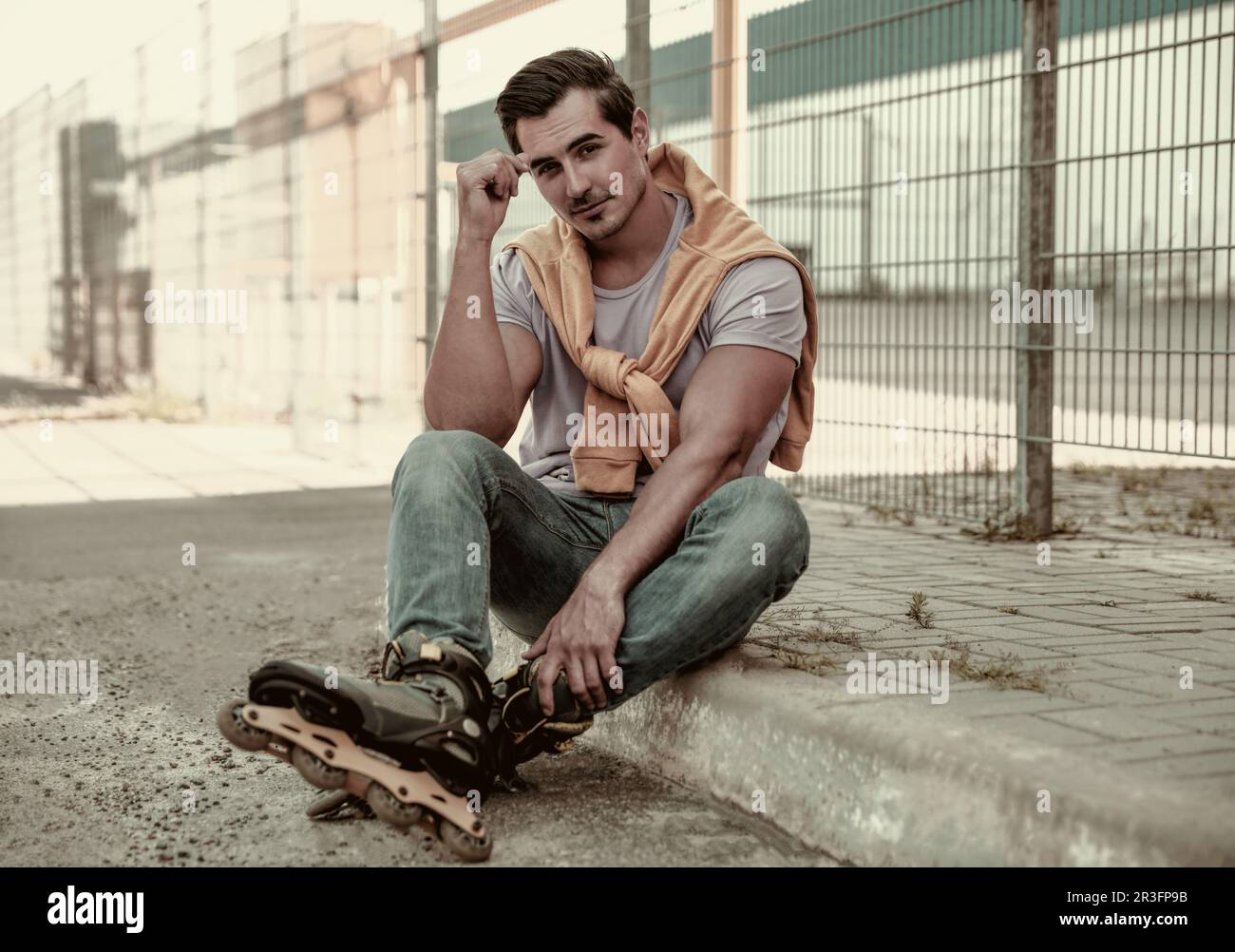Handsome young man with inline roller skates sitting on curb outdoors ...