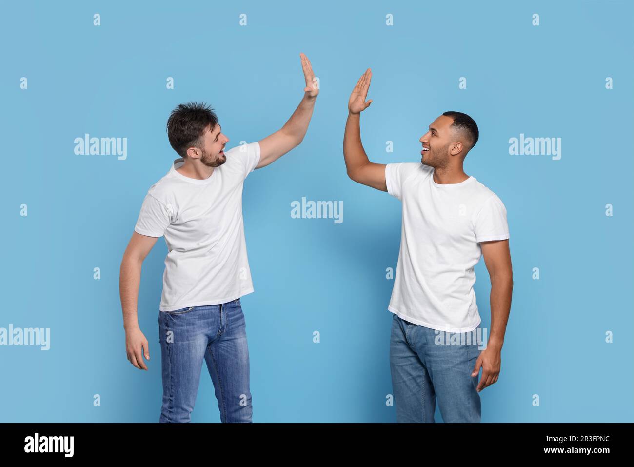 Men giving high five on light blue background Stock Photo - Alamy