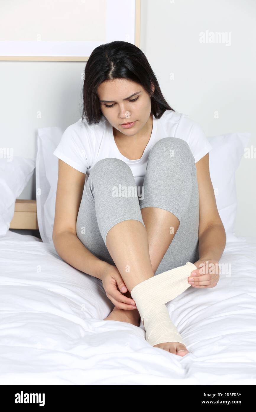 Young woman applying medical bandage onto foot in bedroom Stock Photo ...