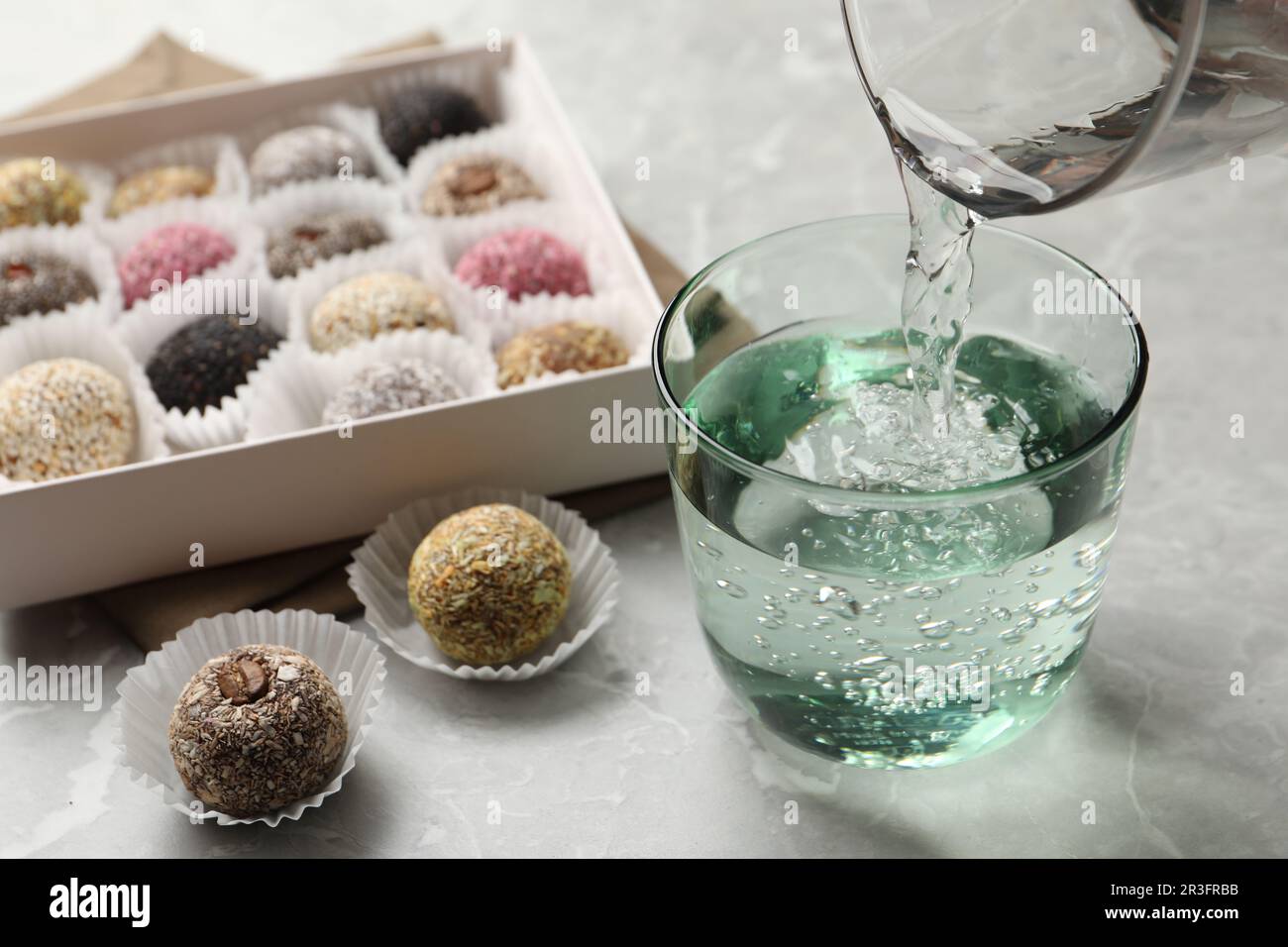 Pouring water into glass and delicious vegan candy balls at light grey ...