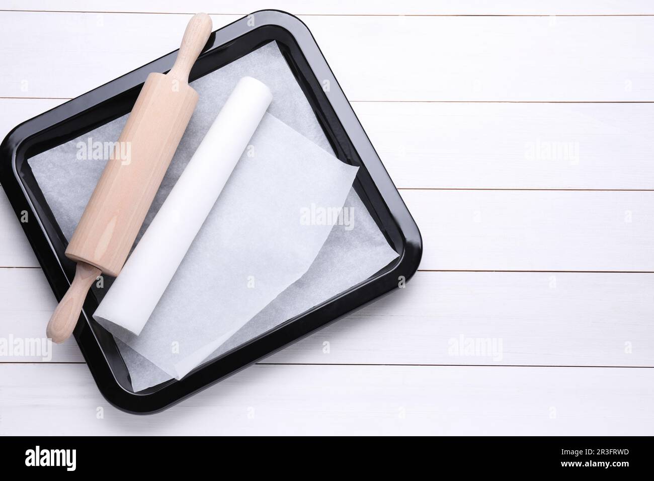 Baking pan with parchment paper and rolling pin on white wooden table ...