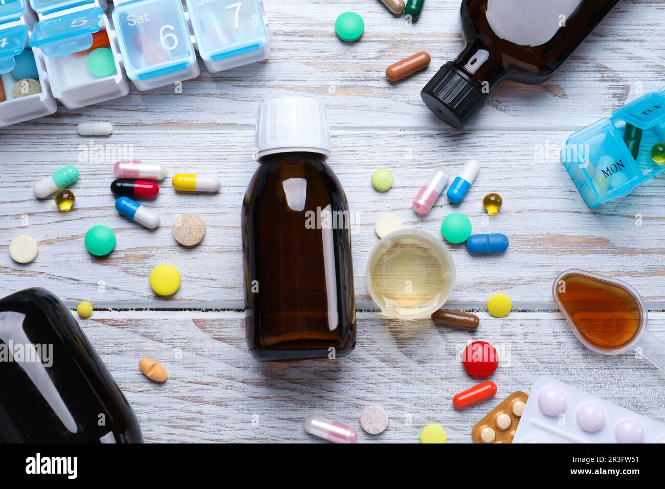 Flat lay composition with bottles of syrup, measuring cup and pills on ...