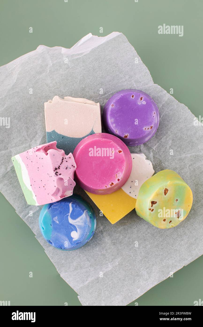 Pieces of different shapes and colors of handmade soap on a green ...