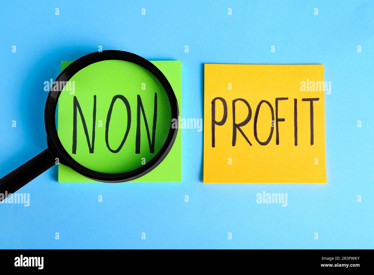 Paper notes with phrase Non Profit under magnifying glass on light blue ...