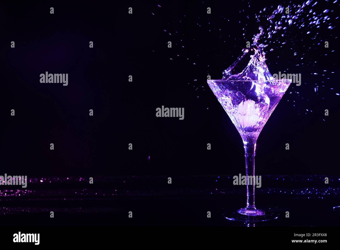 Glass of martini with ice and splashes in neon lights on dark ...