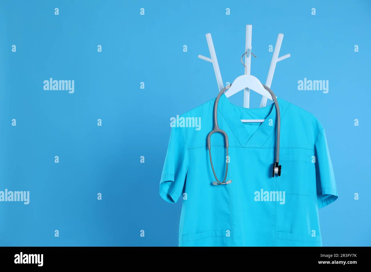 Turquoise medical uniform and stethoscope hanging on rack against light ...
