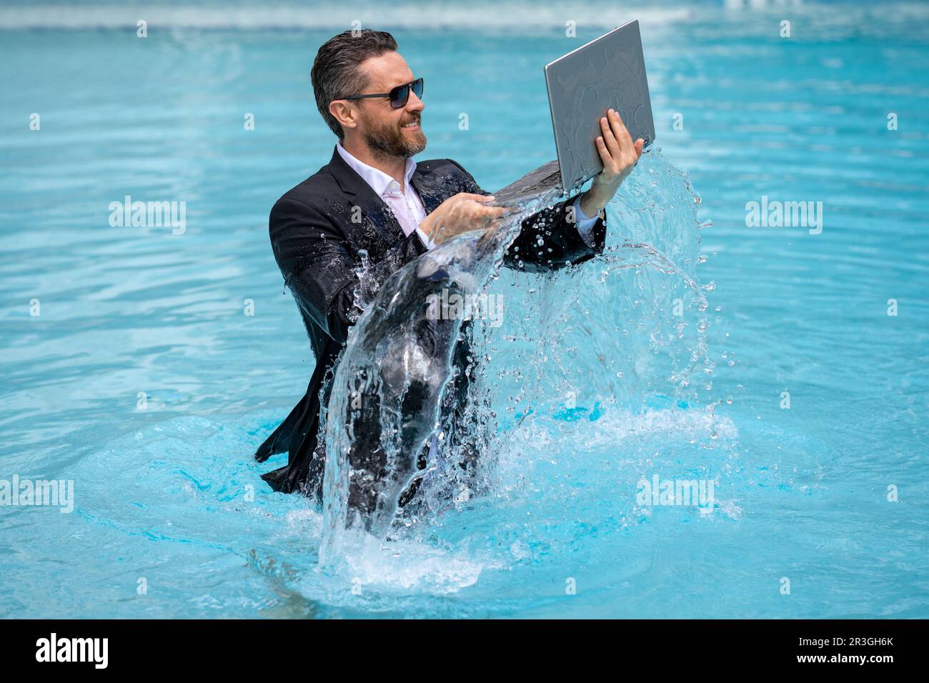 Funny business man in business suit with laptop jumping in splash water ...