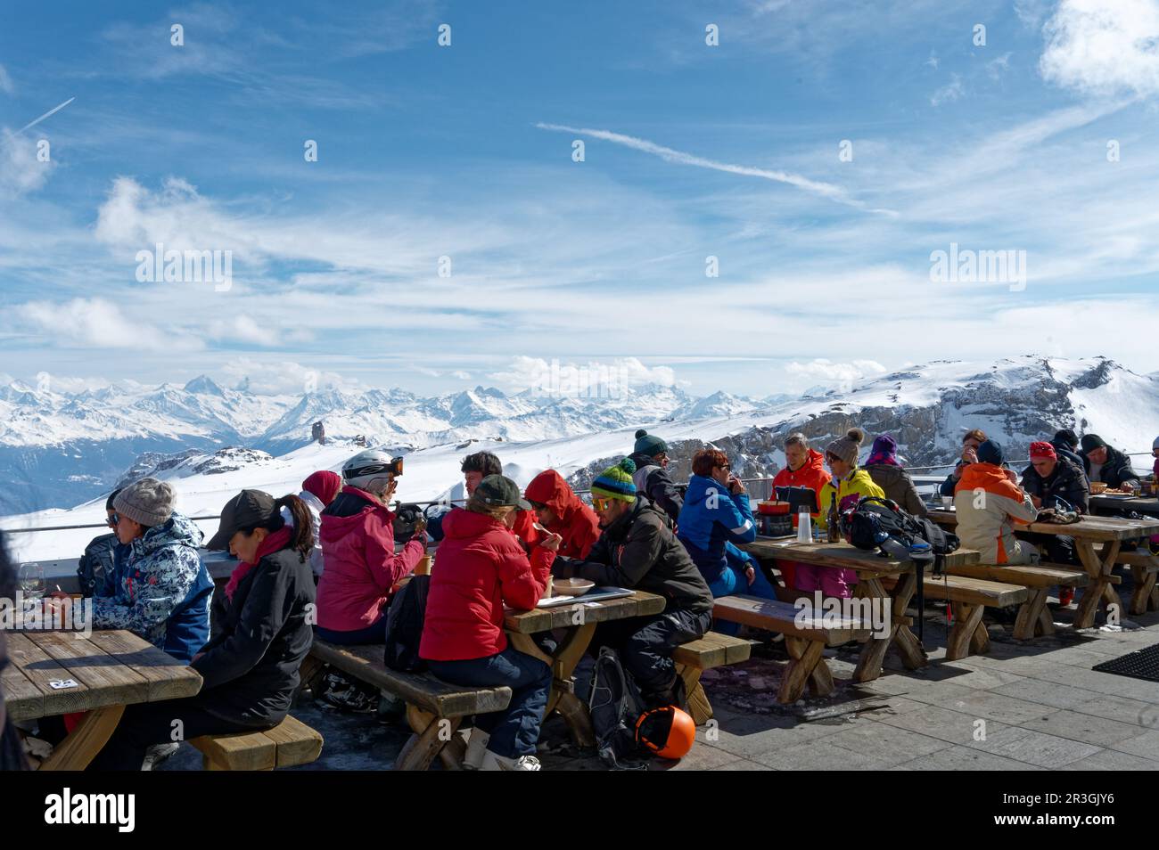 People enjoying the alps while drinking and eating on picnic tables at ...