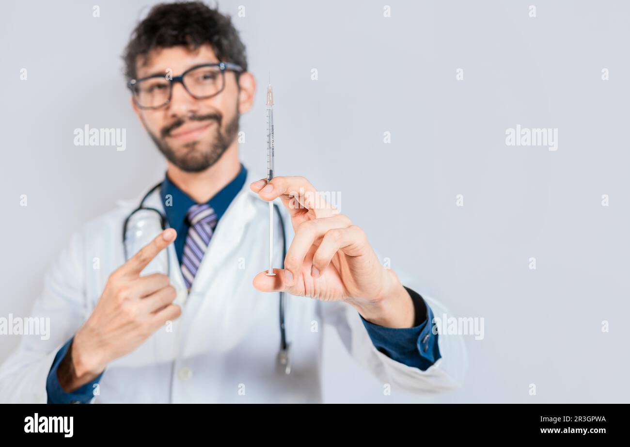 Handsome doctor holding and pointing a syringe isolated. Smiling doctor ...