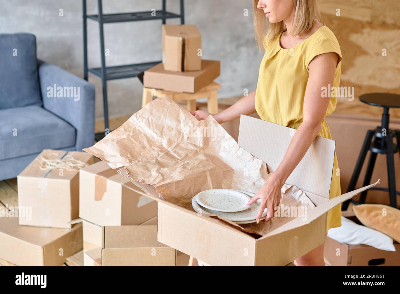Young girl packing plates into the boxes ready to move. Woman unpacking ...