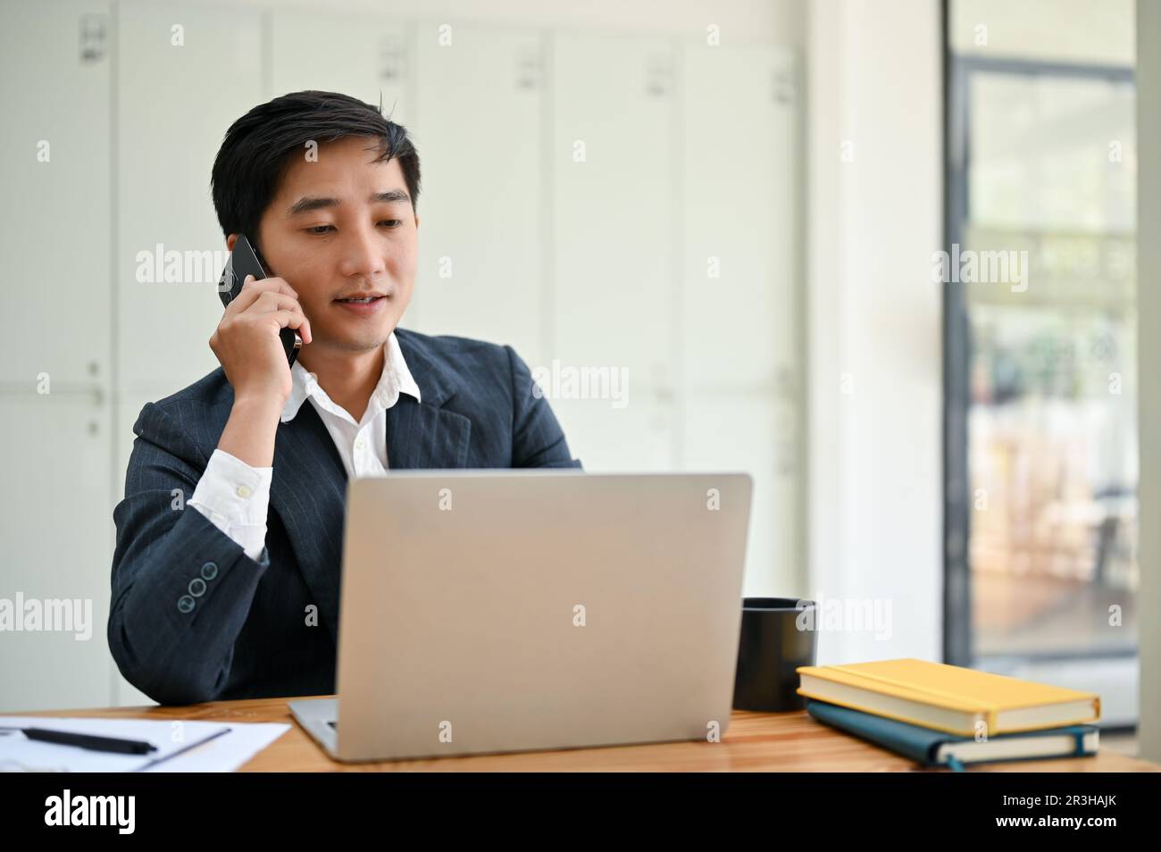 A professional Asian businessman is on the phone, counseling his ...