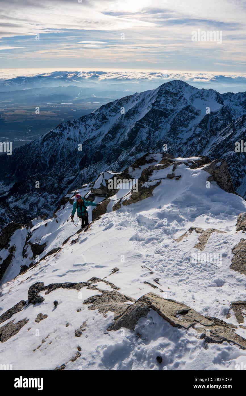 Adventurous man hiker on top of a steep rocky cliff overlooking winter ...