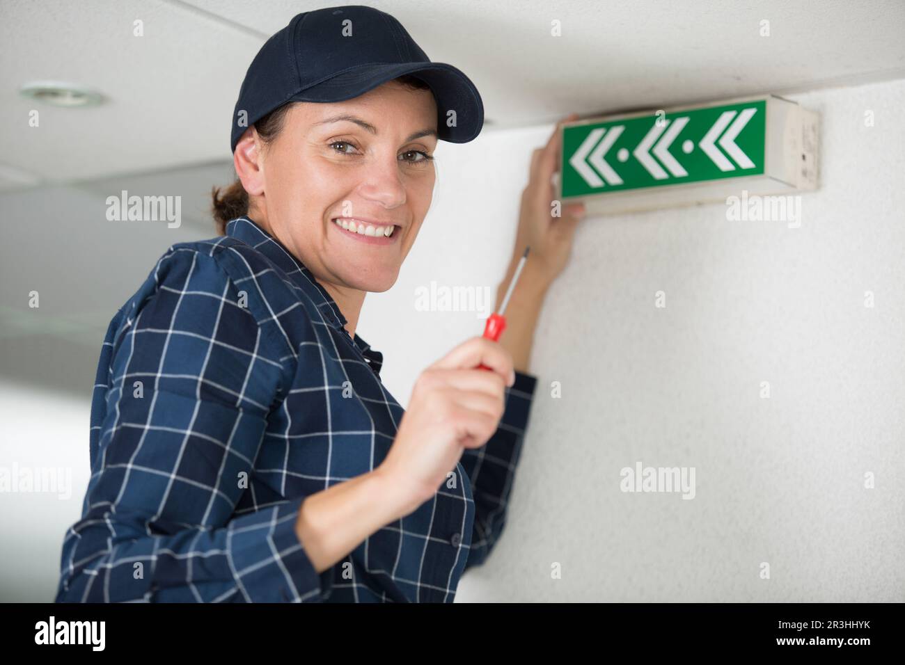 a woman fixing exit sign to wall Stock Photo - Alamy