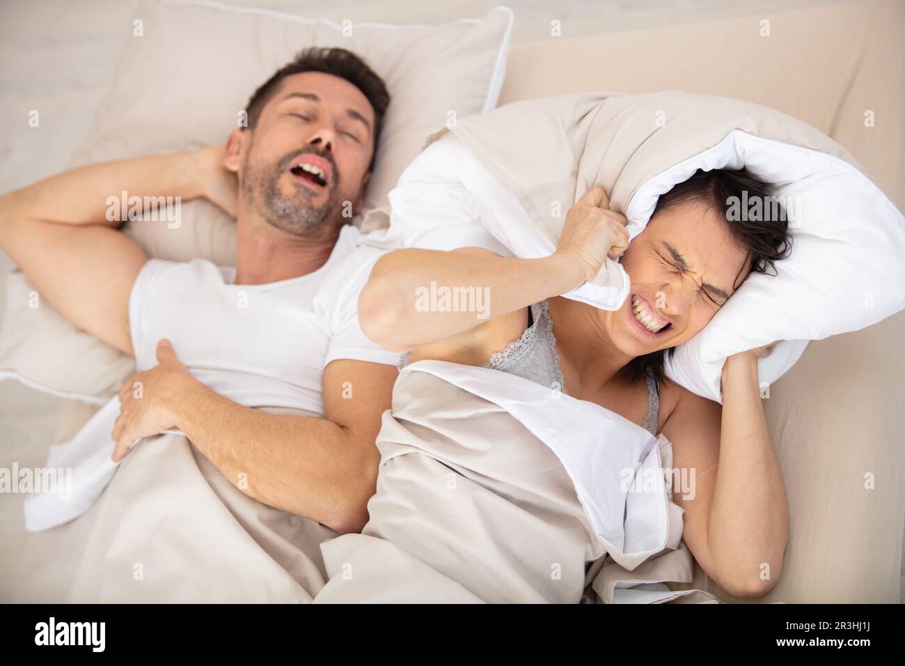 man snoring while his wife is covering ears Stock Photo - Alamy