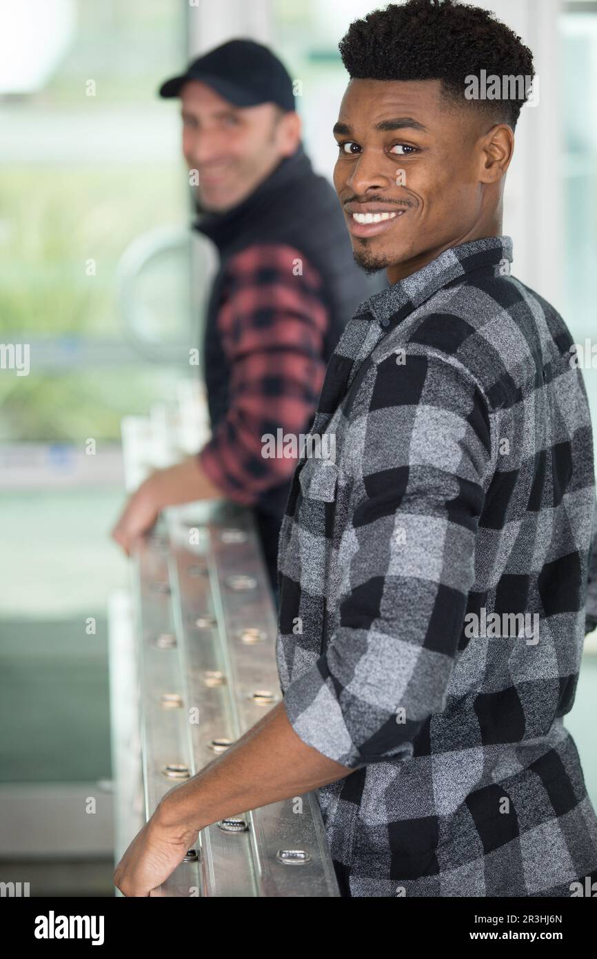 side view of construction workers carrying ladder together Stock Photo ...