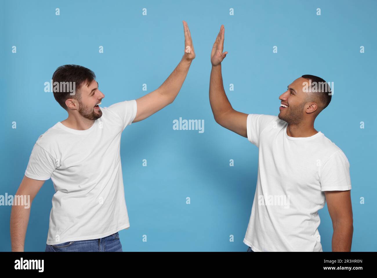 Men giving high five on light blue background Stock Photo - Alamy
