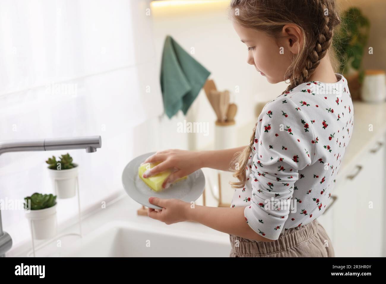 Little girl washing plate above sink in kitchen Stock Photo - Alamy