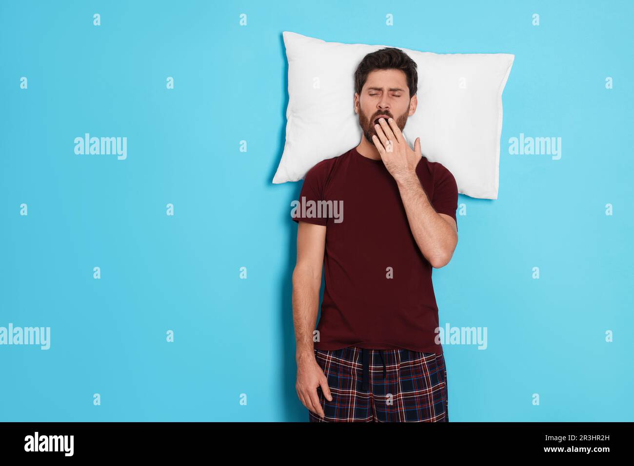 Tired man with pillow yawns on light blue background, space for text ...