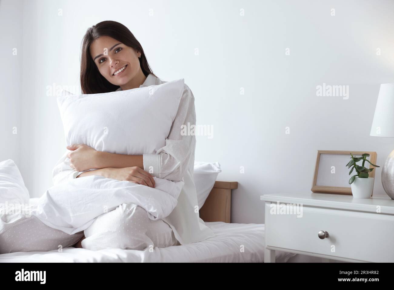 Beautiful young woman hugging pillow on bed at home Stock Photo - Alamy