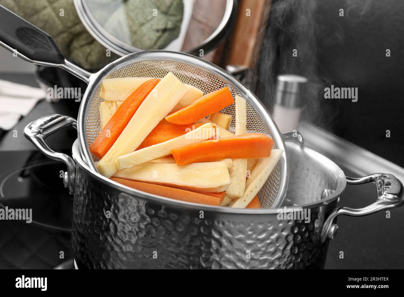 Putting cut parsnips and carrots into pot with boiling water in kitchen ...