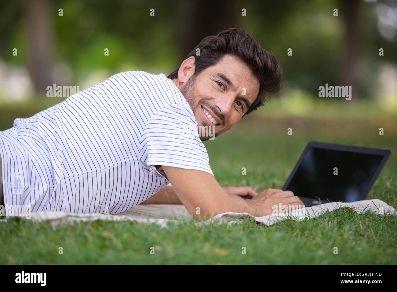 man laying down on green grass using a laptop computer Stock Photo - Alamy