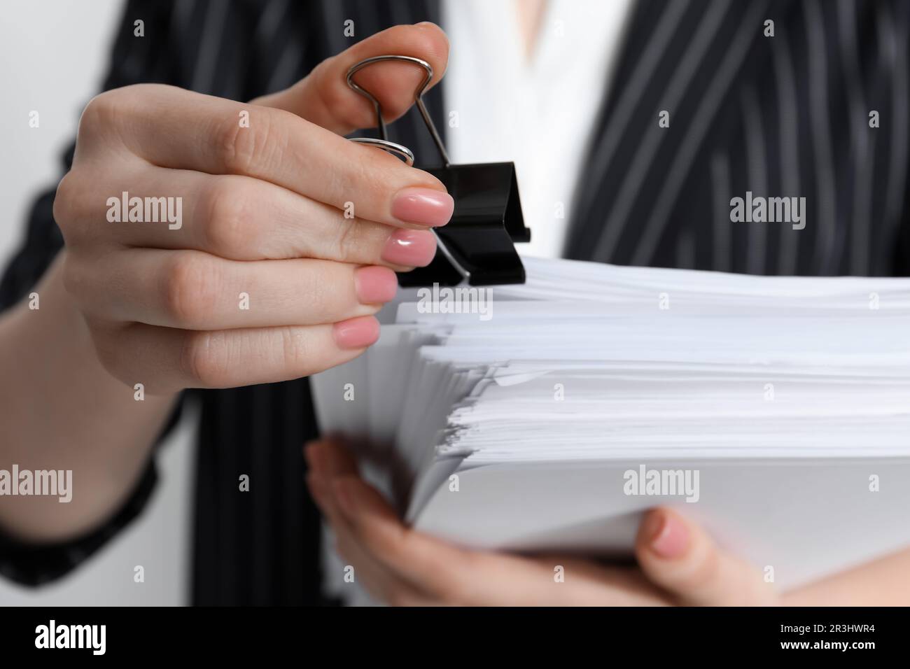 Woman attaching documents with metal binder clip on grey background ...