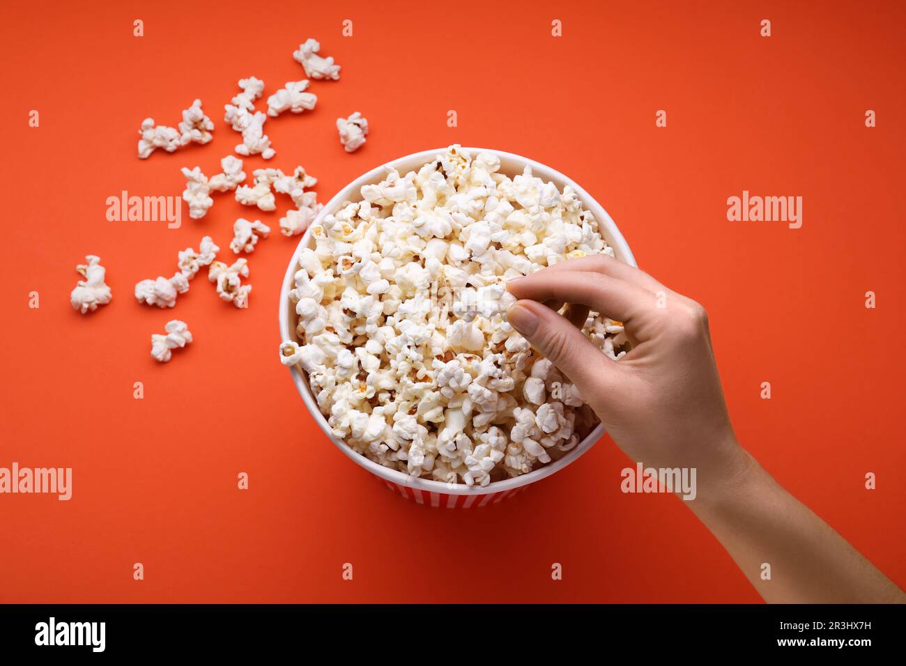 Woman taking fresh popcorn from bucket on orange background, above view ...